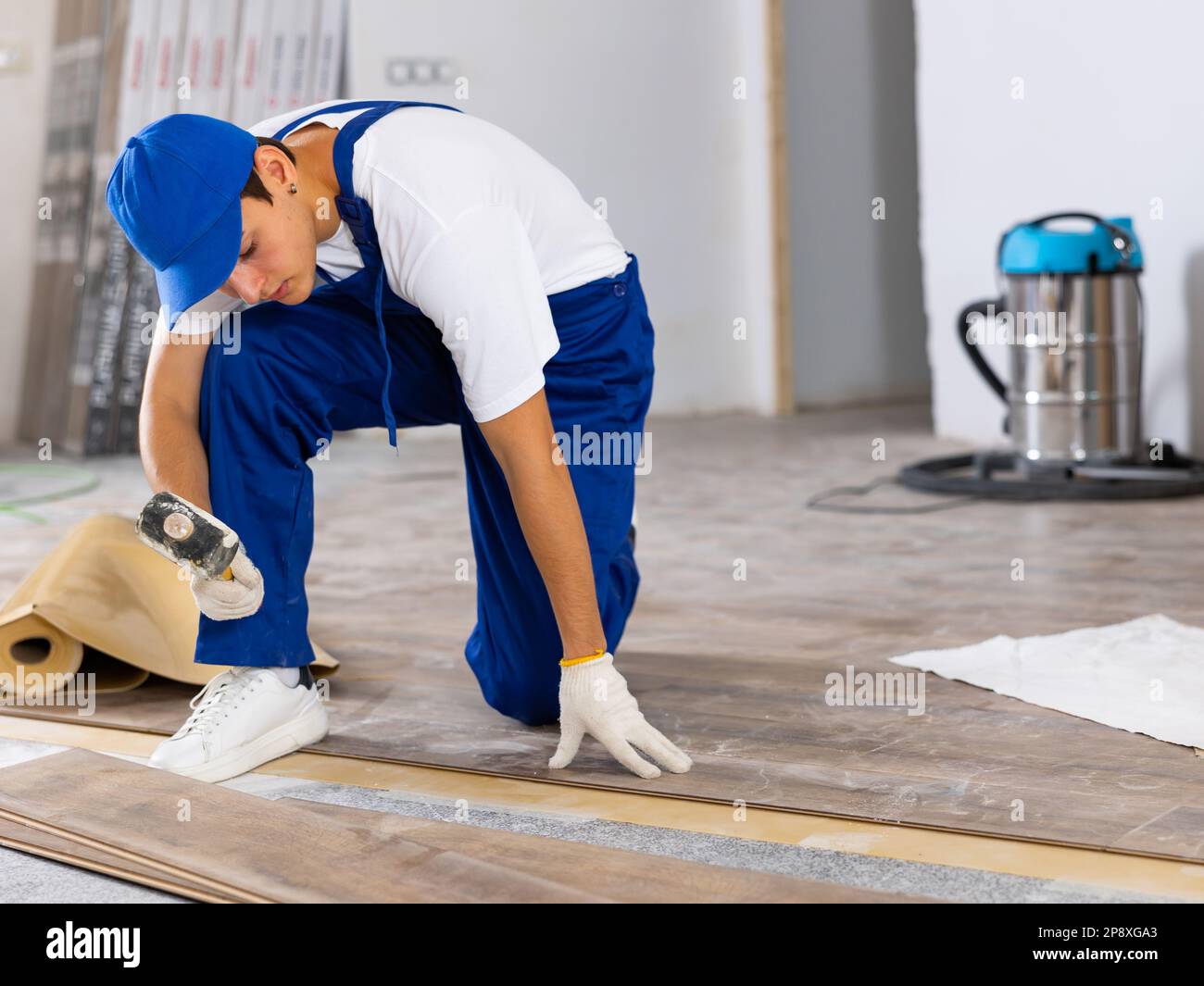 Young carpenter using rubber mallet to lay laminate flooring indoors ...