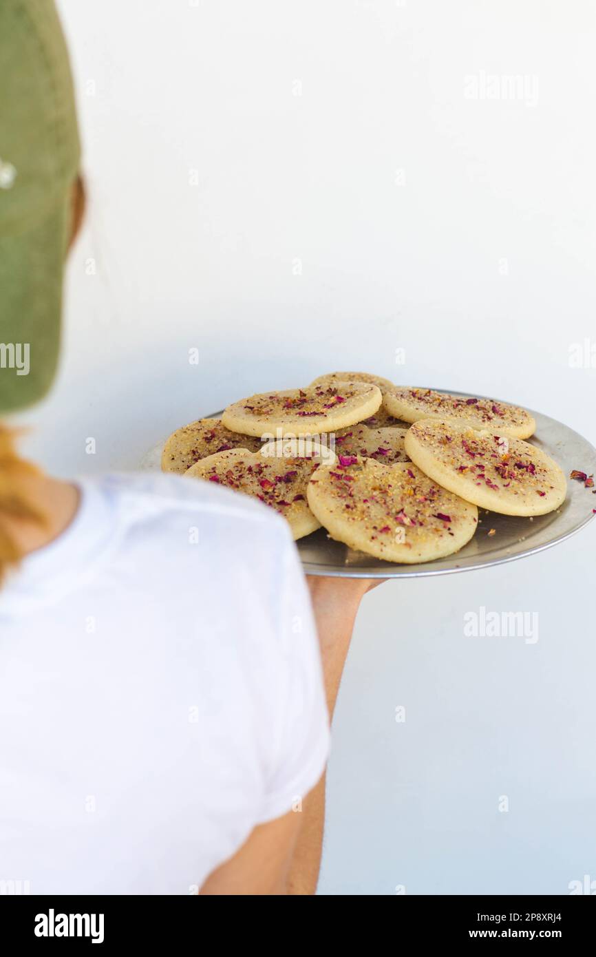 A baker holds a tray of cookies seen over her shoulder on a simple ...