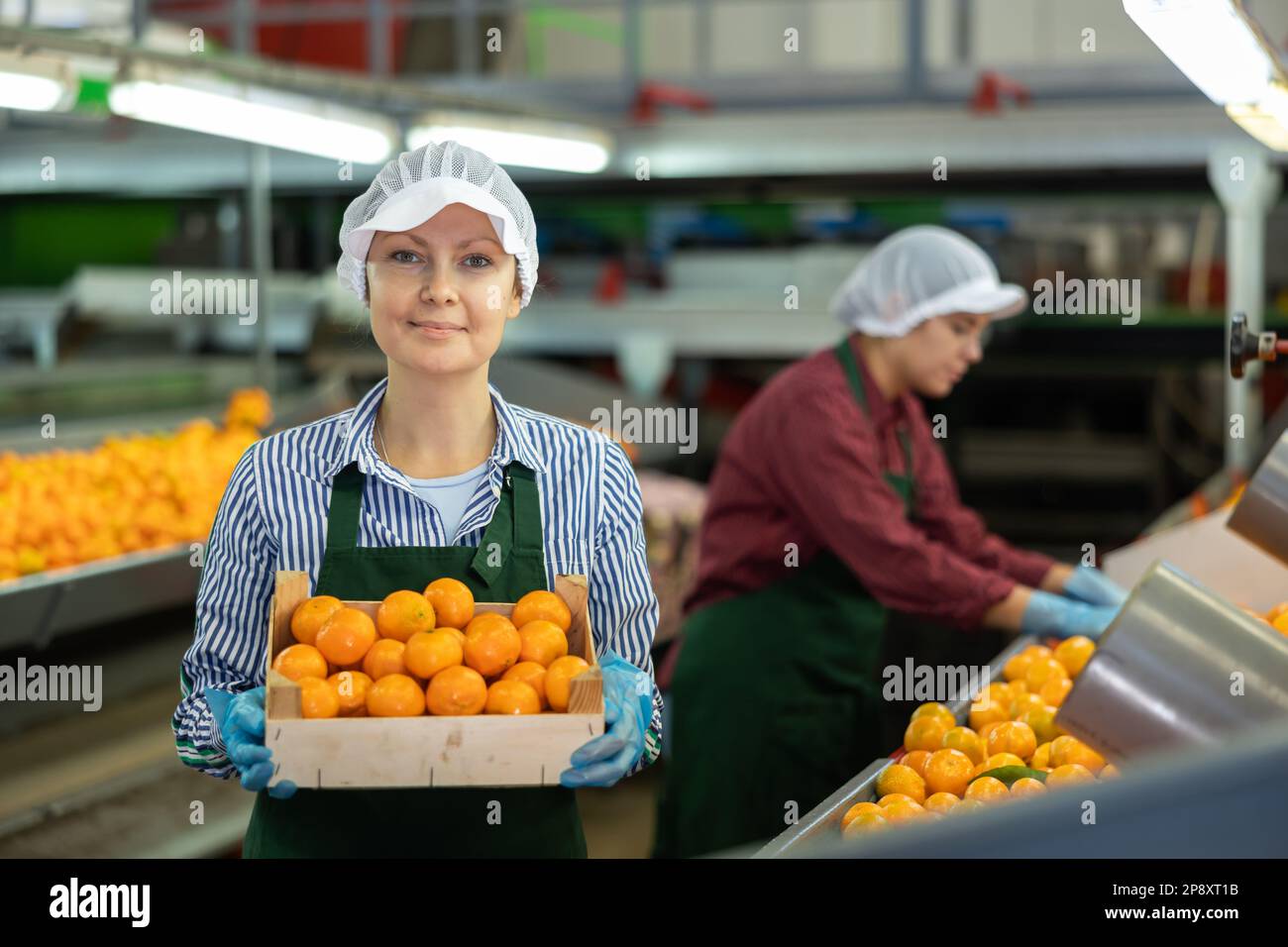 Glad positive female employee in colored uniforms hold a box of fresh ...