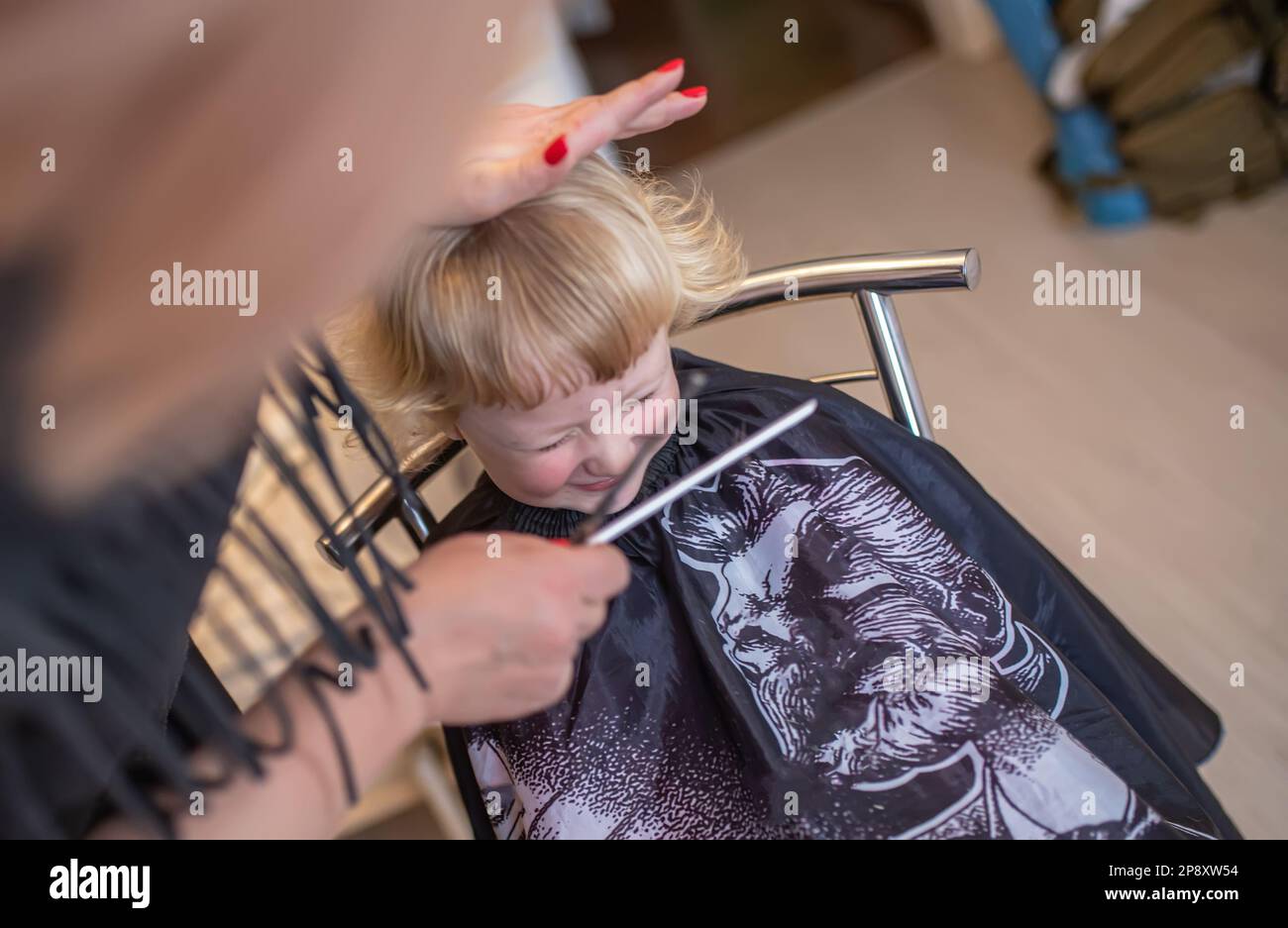 The little girl squinted her eyes on the hairdresser's chair. combing a girl's hair in a ...