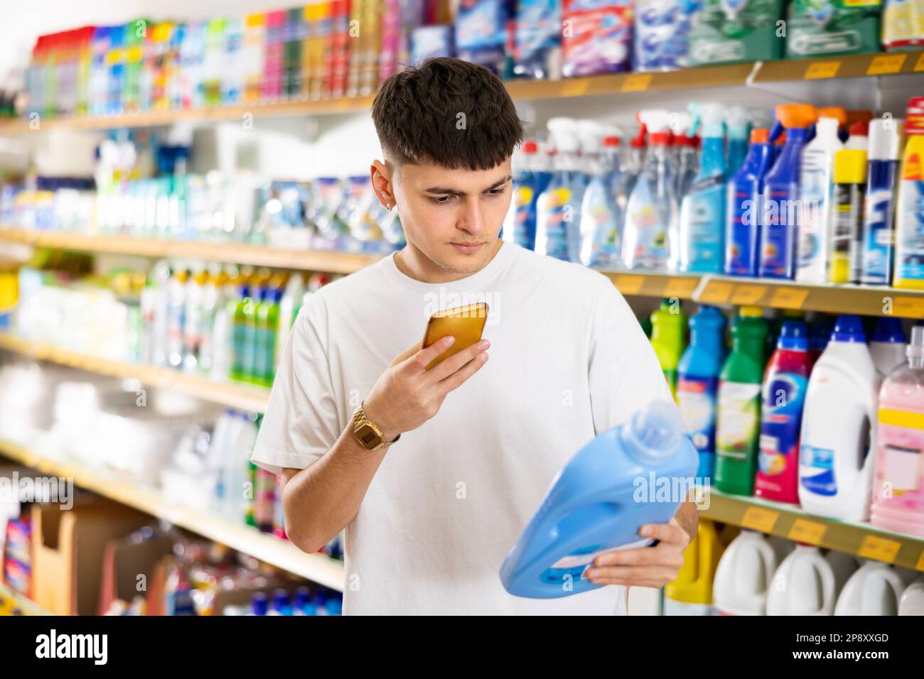 Young man scanning qr-code on bottle of laundry detergent in ...
