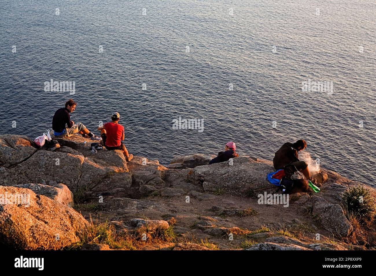 Pilgrims in Cape Finisterre enjoying a sunset. At right pilgrim burning ...