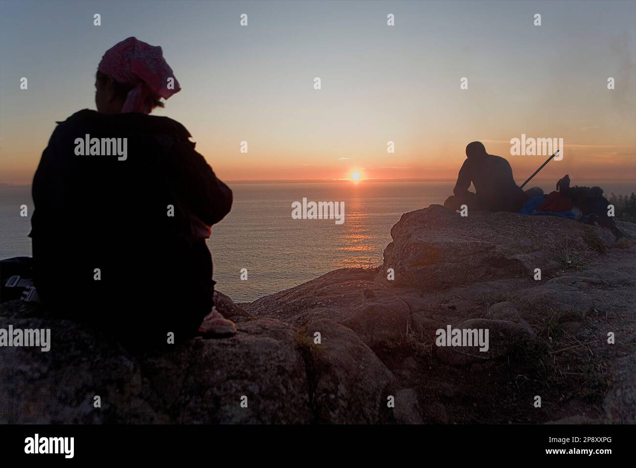 Pilgrims in Cape Finisterre enjoying a sunset. At right a pilgrim burn ...