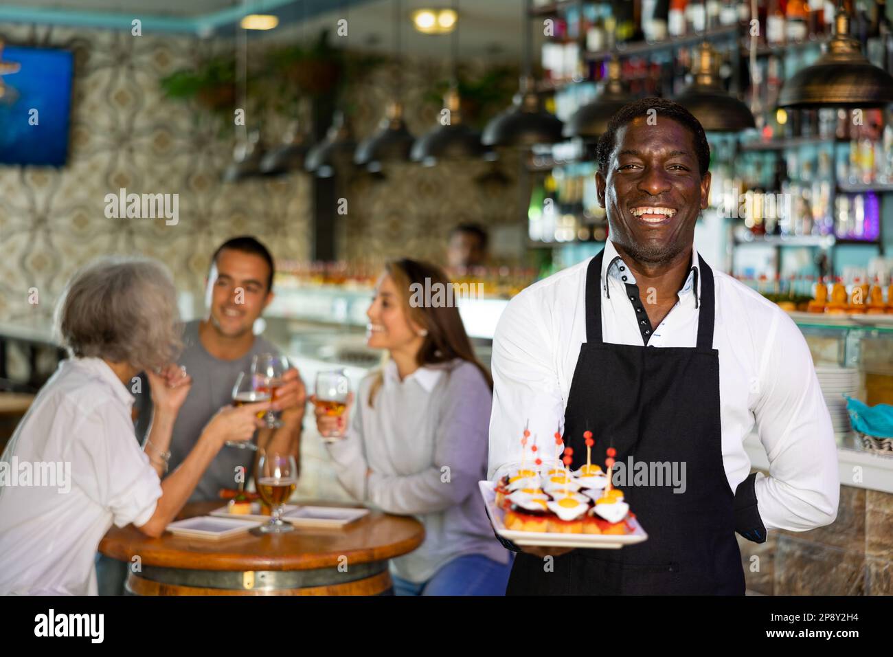 Positive African American waiter serving tapas for friends meeting for ...