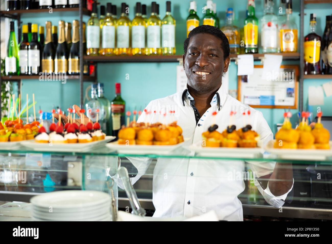 Smiling African American bartender standing with plates of pinchos in ...