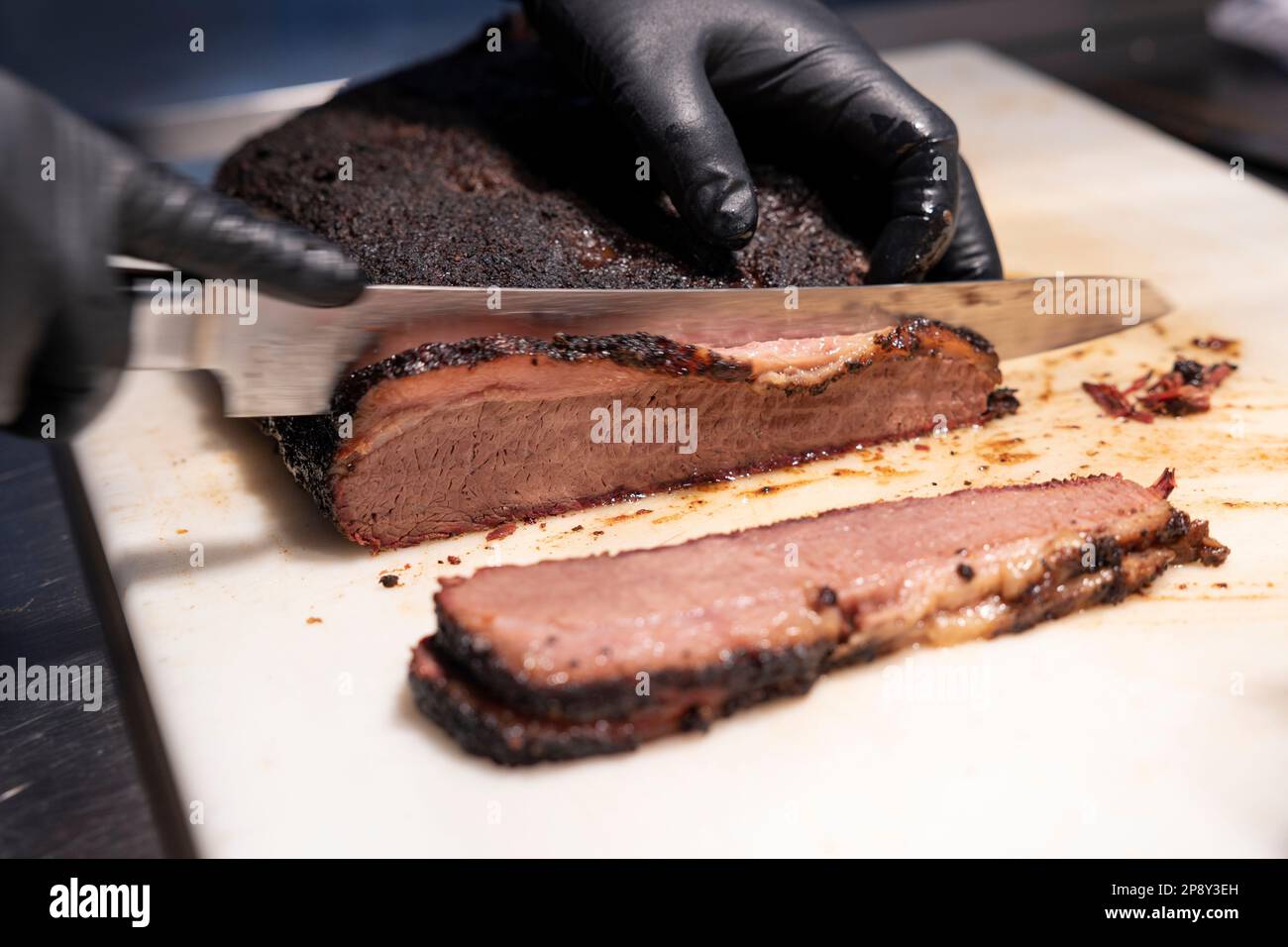 Beef brisket being sliced with a knife into strips on a white cutting ...