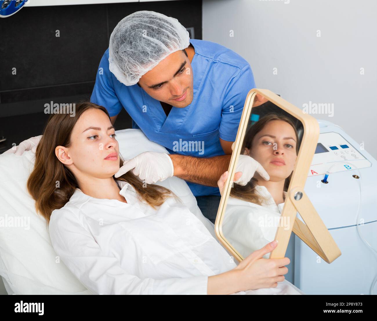 Female client looking at mirror while beautician examining her face ...