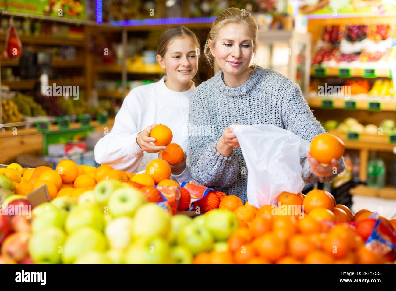 Portrait of teenage girl and mother who buying fresh oranges at grocery ...