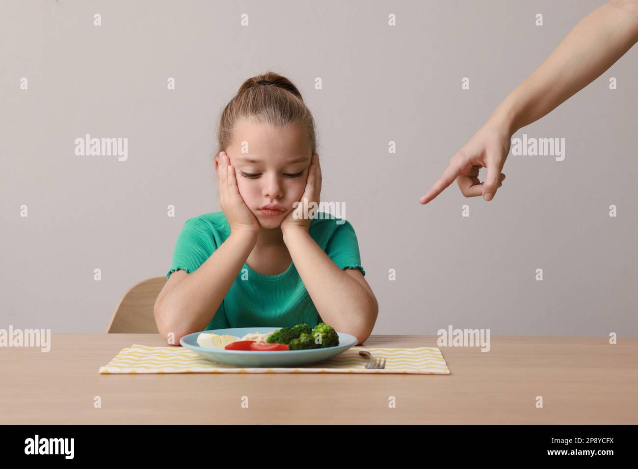 Cute little girl refusing to eat her breakfast at table on grey ...