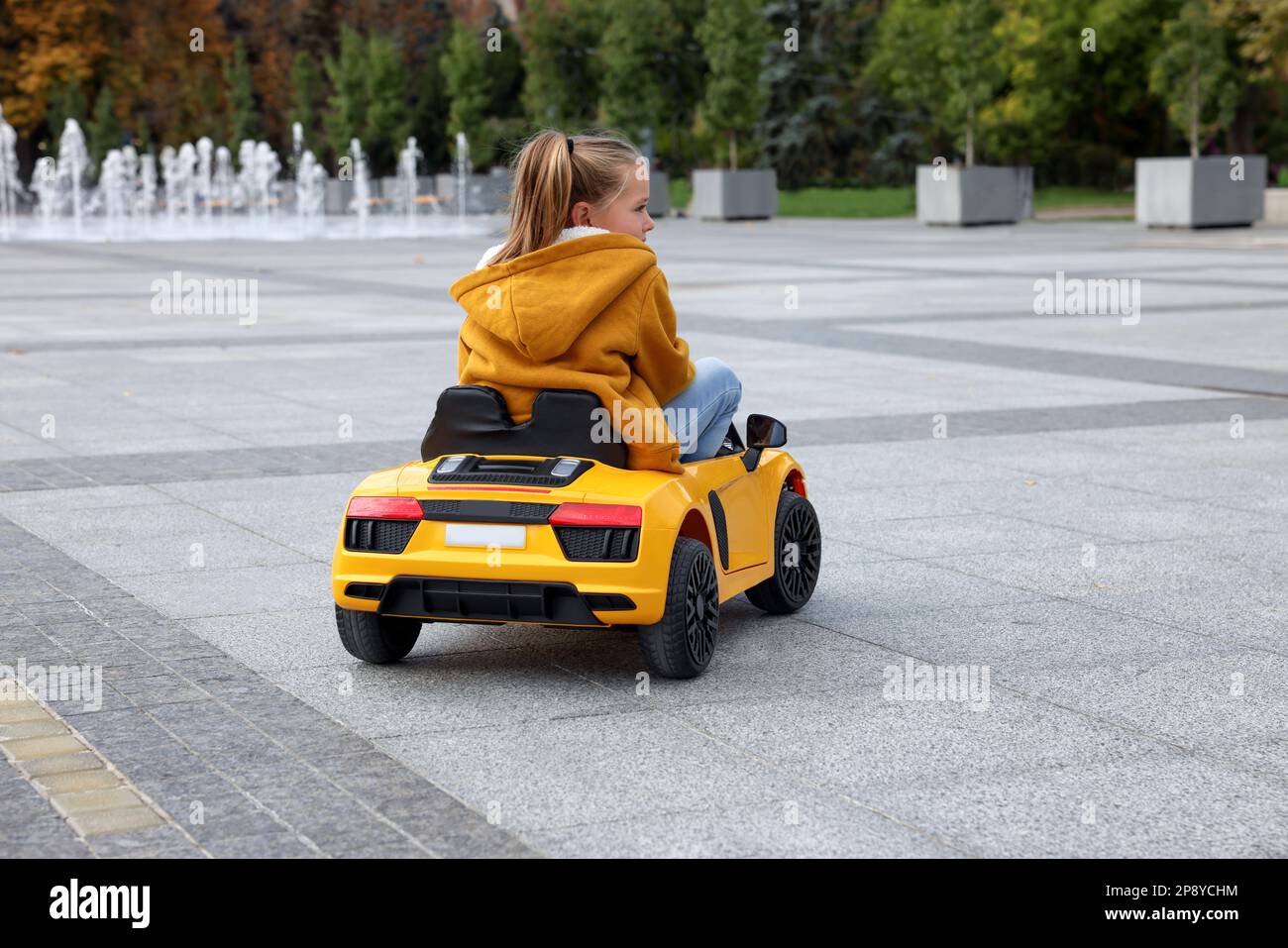 Cute little girl driving children's car on city street, back view Stock ...