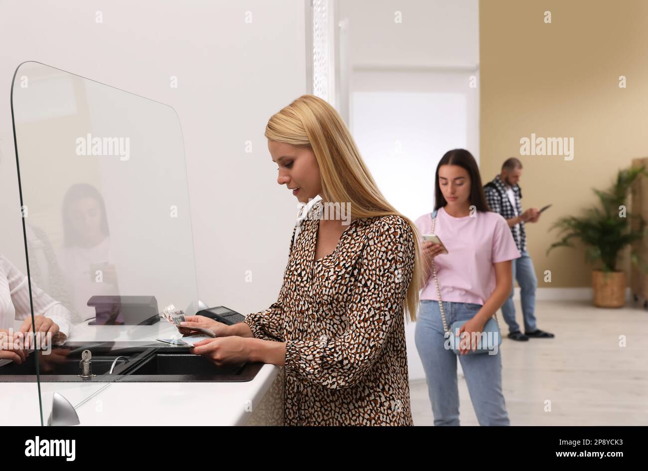Woman with money and other people in line at cash department window ...