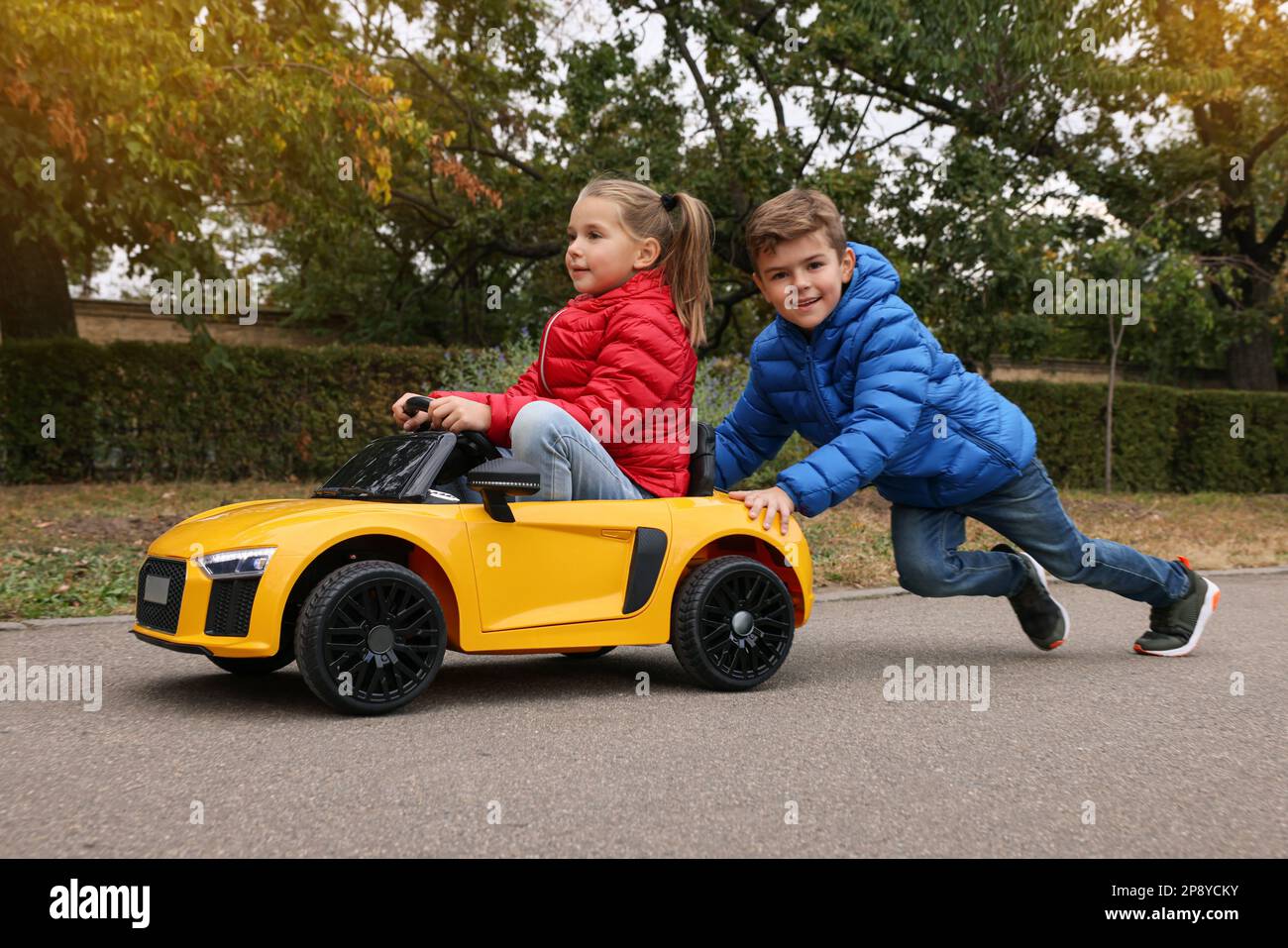 Cute boy pushing children's car with little girl outdoors Stock Photo ...
