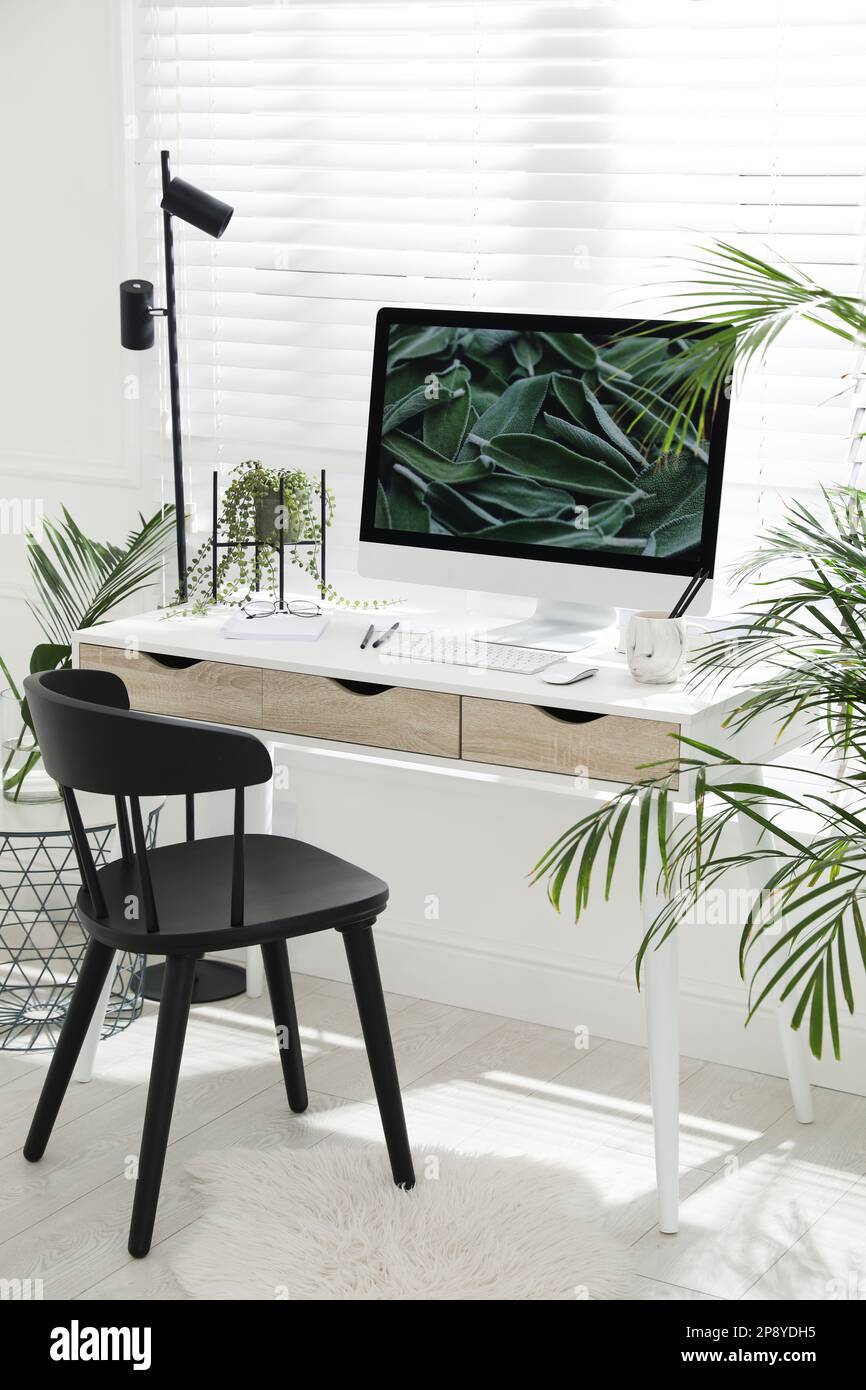 Comfortable workplace with modern computer and green plants in room ...