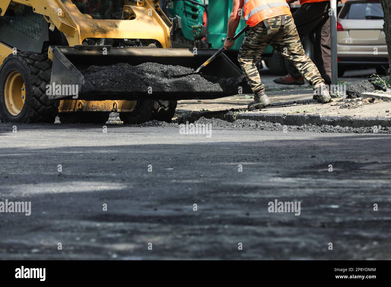 Worker laying new asphalt with skid loader on city street, closeup ...