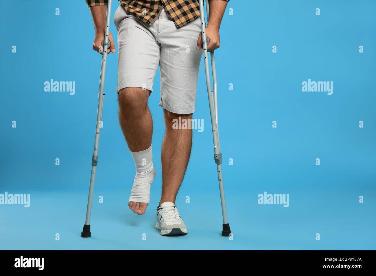 Young man with injured leg using axillary crutches on light blue ...