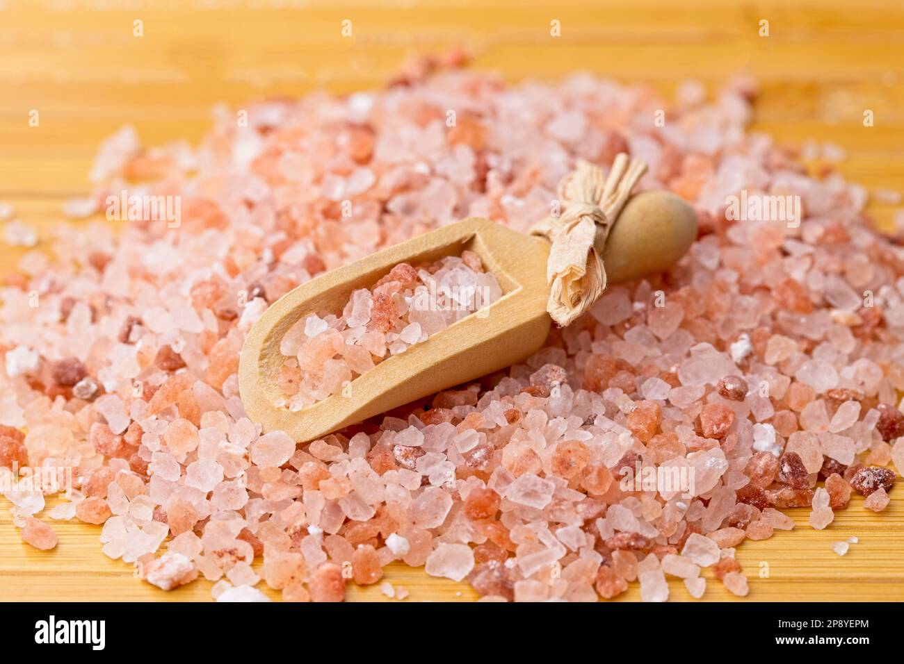 A close up image of a small wooden scoop on a pile of raw pink ...