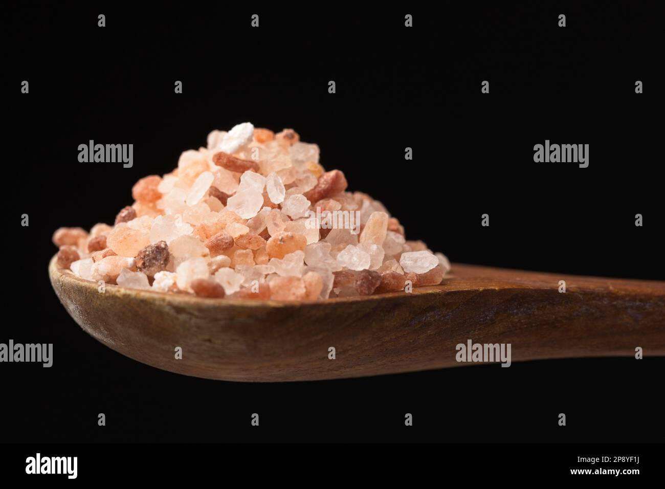 A close up photo of coarse himalayan sea salt on a wooden spoon against ...