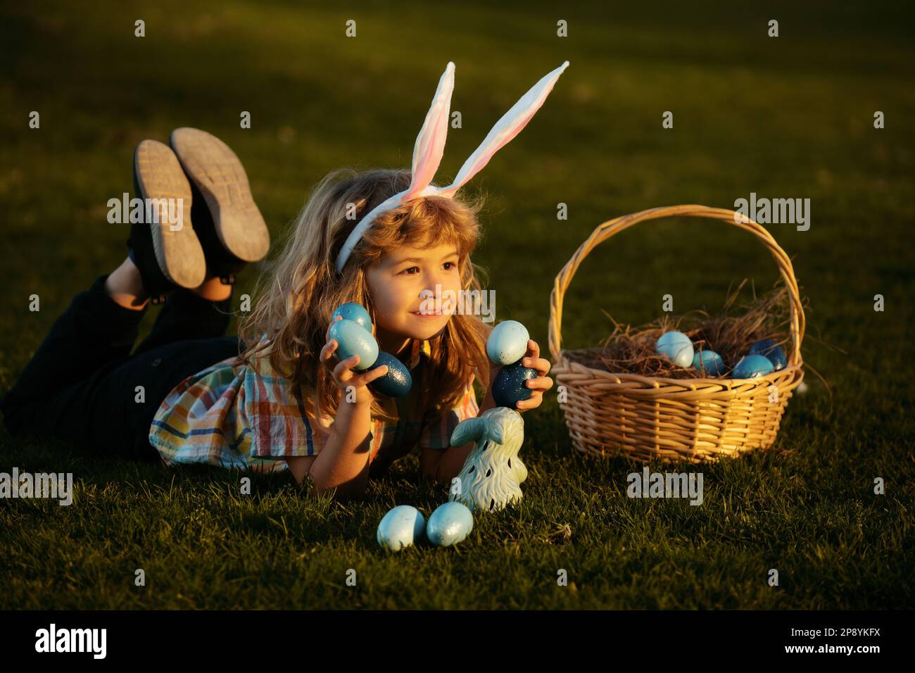 Child with easter eggs in basket outdoor. Boy laying on grass in park ...