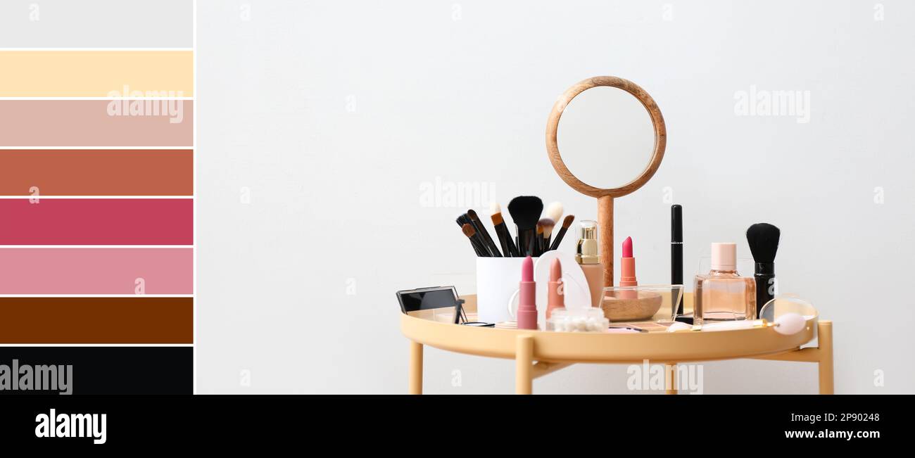 Set of makeup cosmetics with brushes and mirror on table against light ...