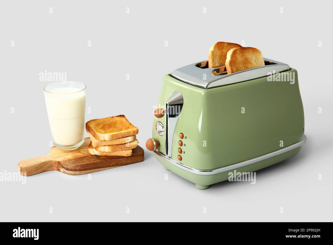 Bread slices in modern toaster, glass of milk and tasty toasts with jam on white background ...