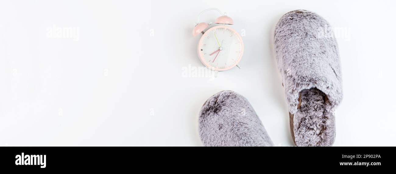 Flat lay with Soft fluffy slippers gray color and pink alarm clock ...