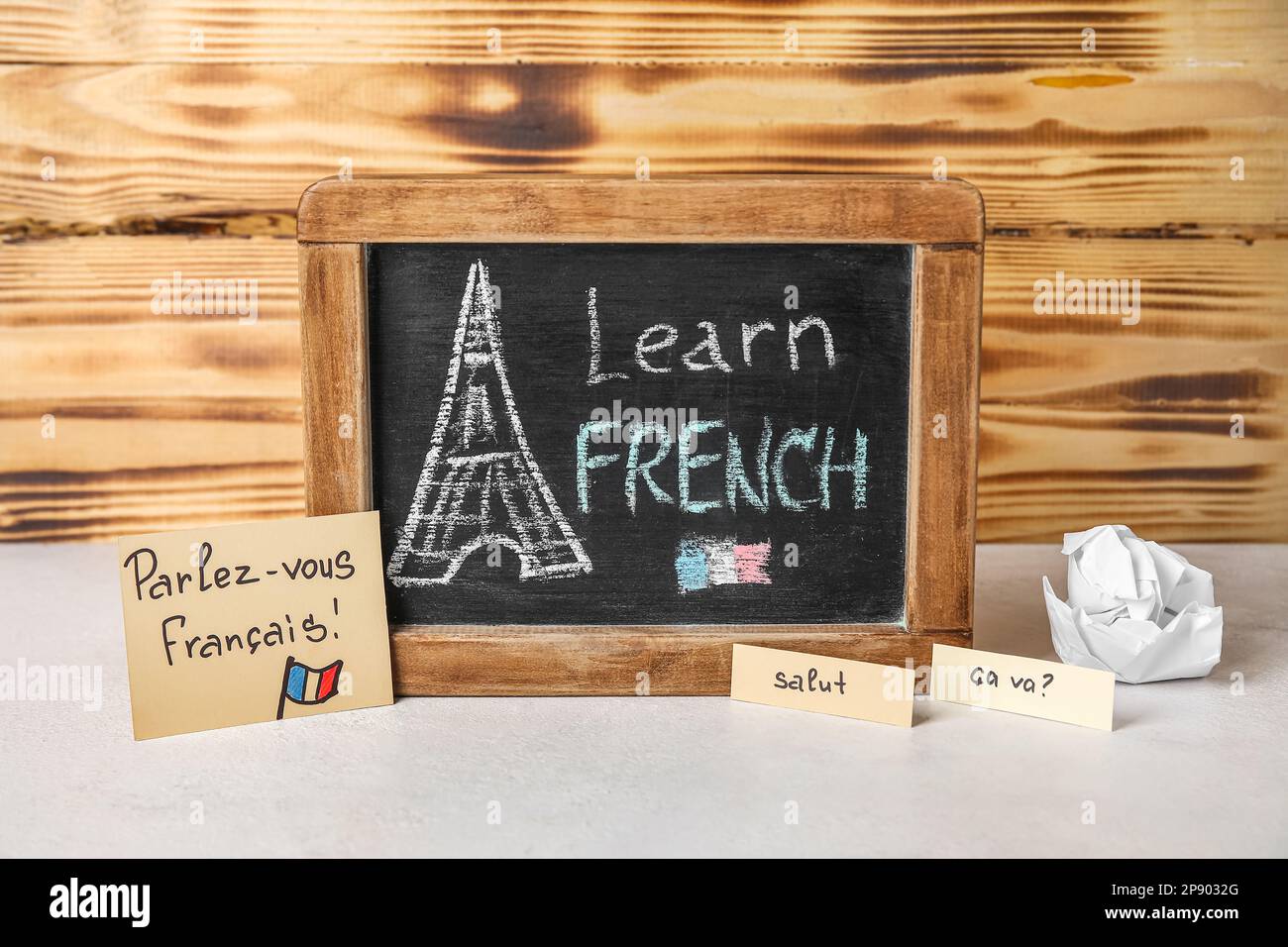 Chalkboard with text LEARN FRENCH, words and crumpled paper on table ...