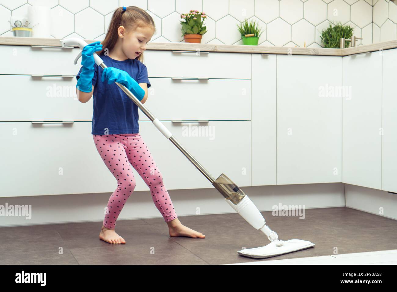 Pretty little girl in household gloves wash floor with modern mop with ...