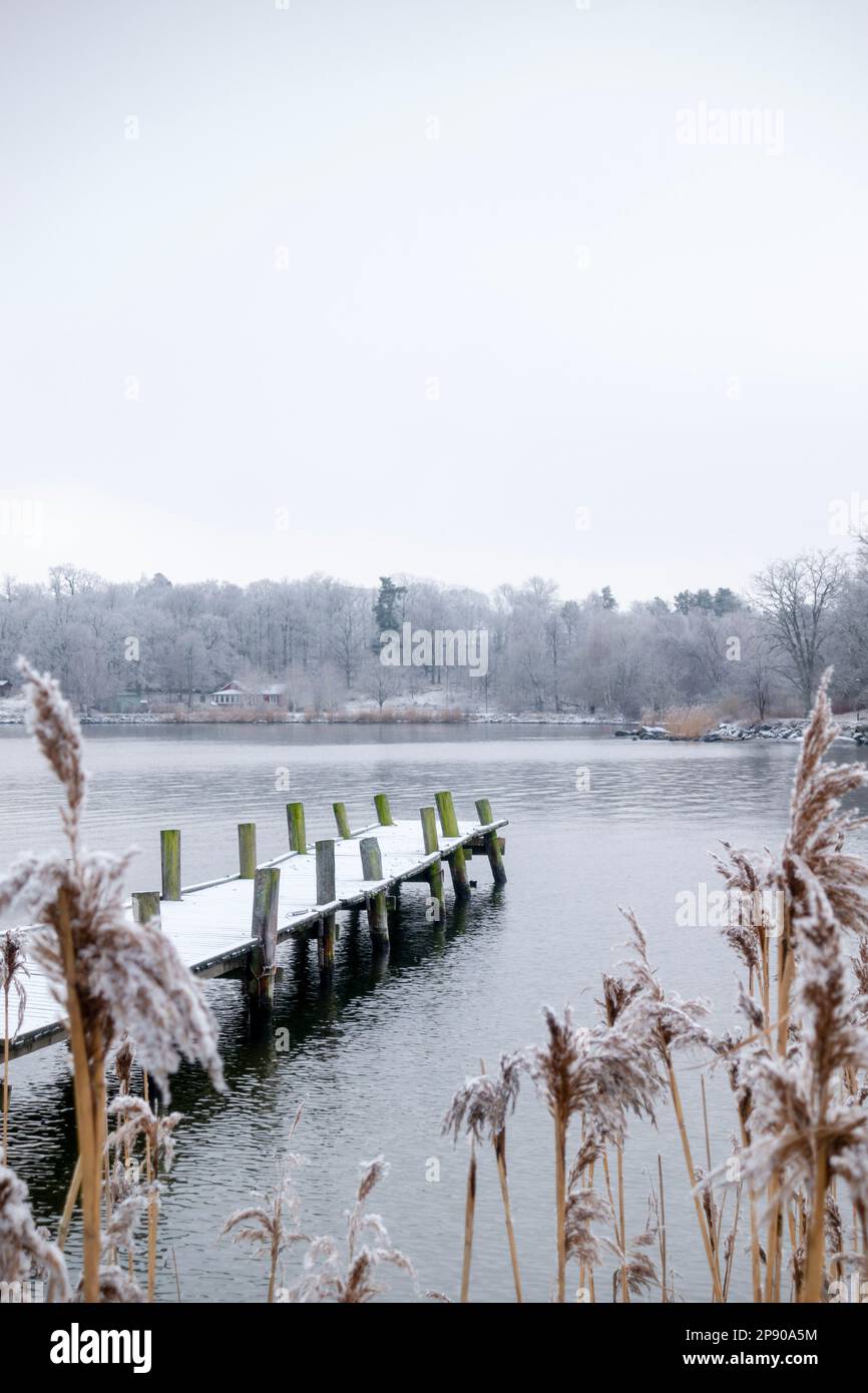 Snow covered wooden jetty in frozen calm water lake with calming orange ...