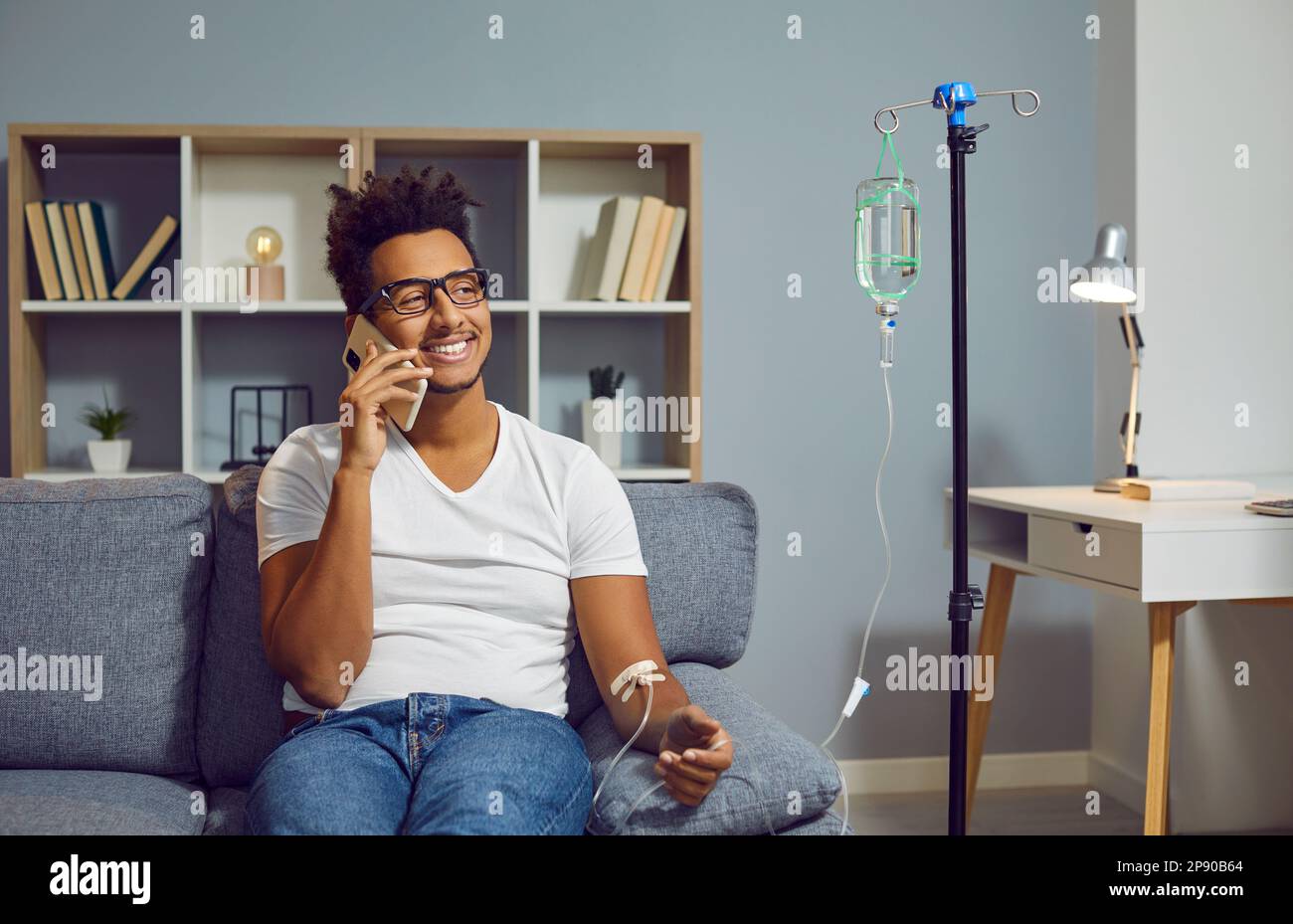 Happy man sitting on sofa at home, receiving intravenous drip infusion ...