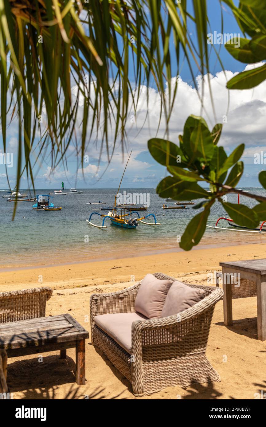 Views of Sanur beach, boats, ocean, trees. Cafe tables on the sand ...