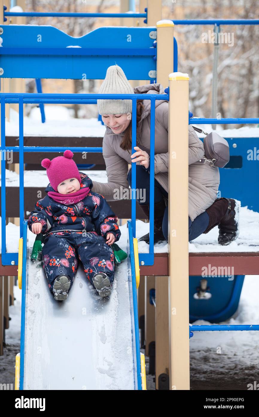 Mom helps a small child slide down the slide on the playground ...