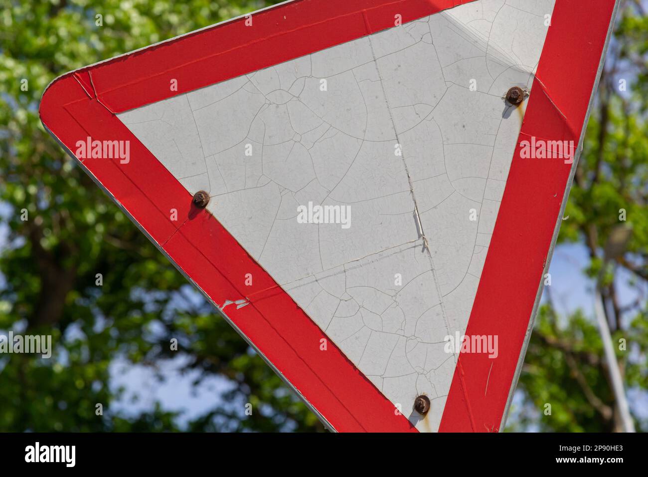 Close-up of give way road sign. Red and white triangle. Green trees and ...