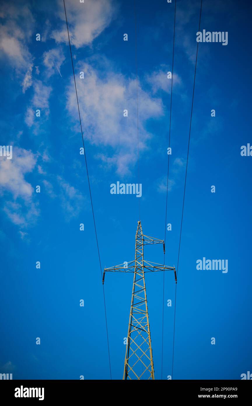 High voltage power cables suspended on a metal pole against a blue sky ...