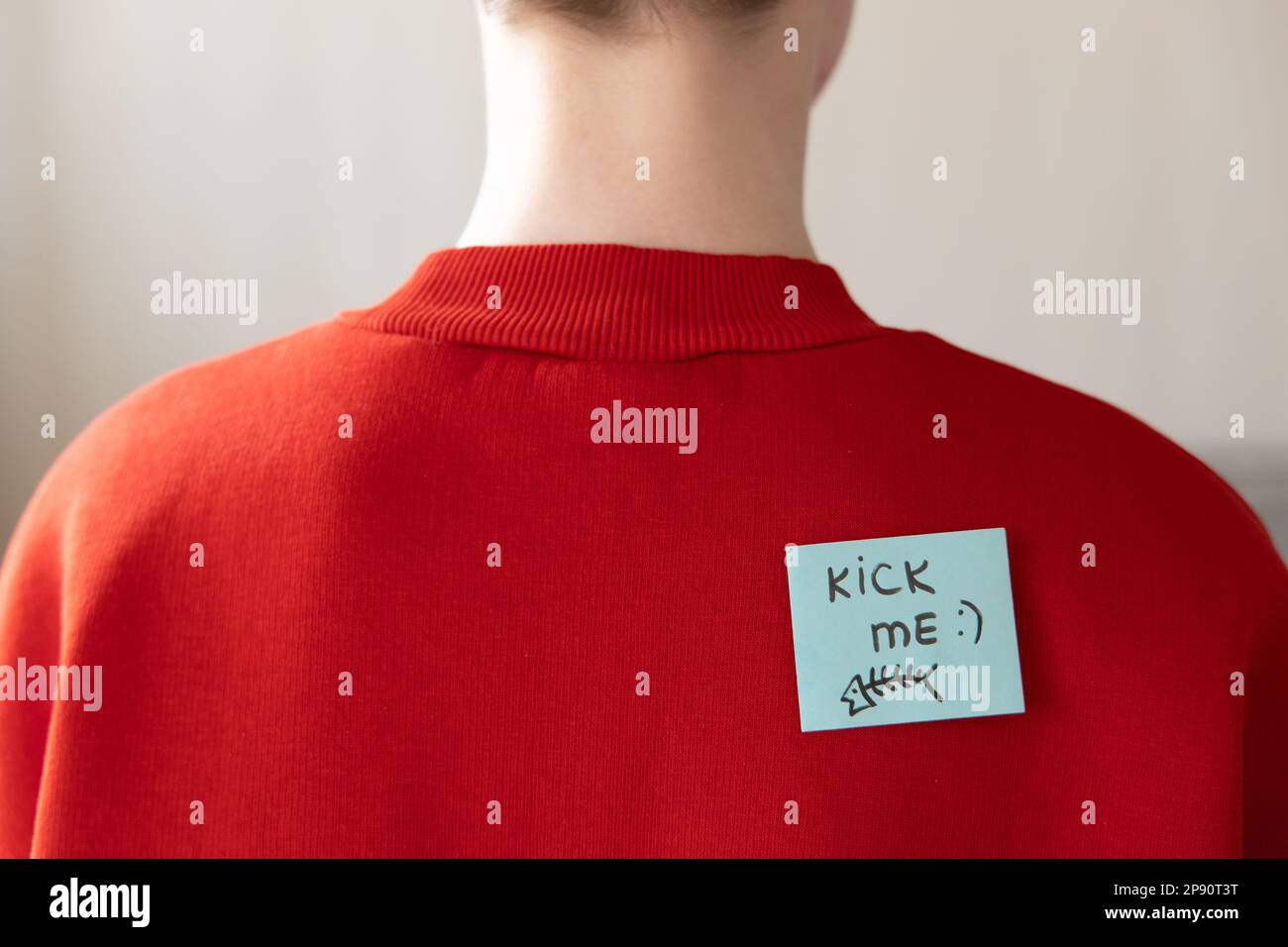 Boy in red hoodie with a sticky note on his back, saying kick me Stock ...