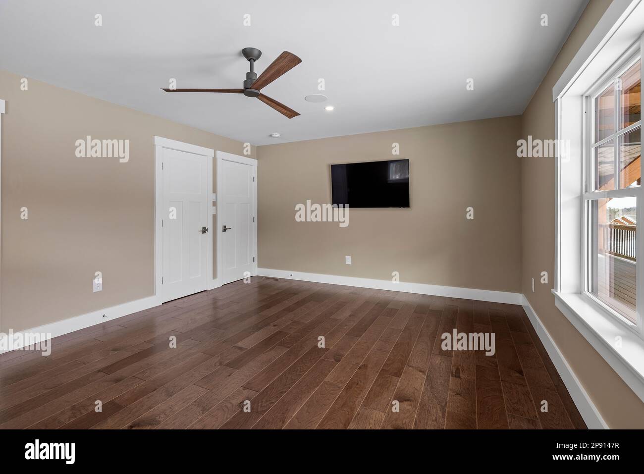 An empty room with a ceiling fan, hardwood floor and large windows ...