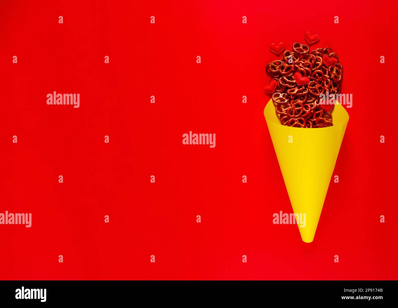 Mini Pretzels And Small Colorful Hearts In Yellow Paper Cone Lie On Red