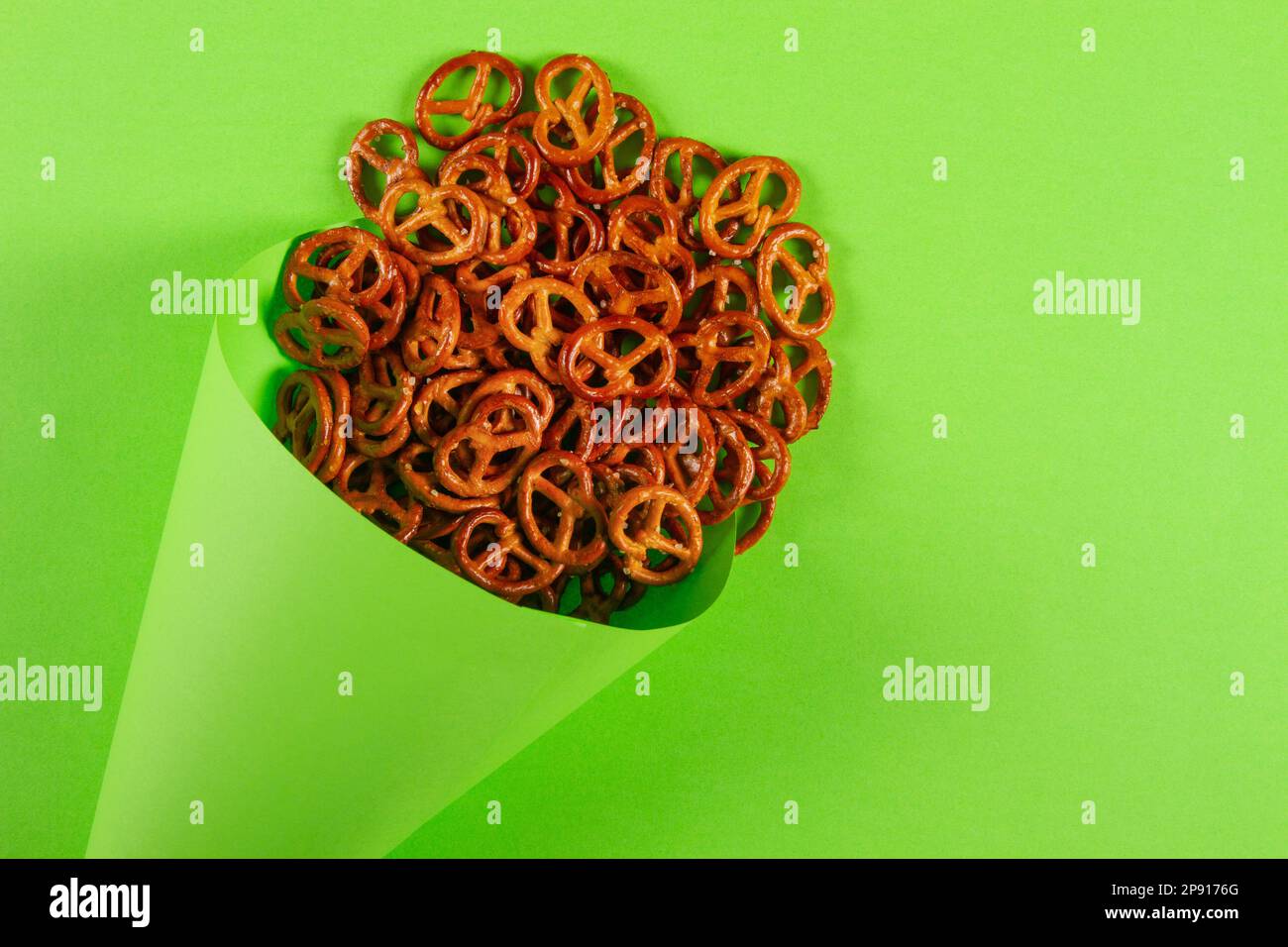 Mini pretzels in light green paper cone lie on bright green background ...