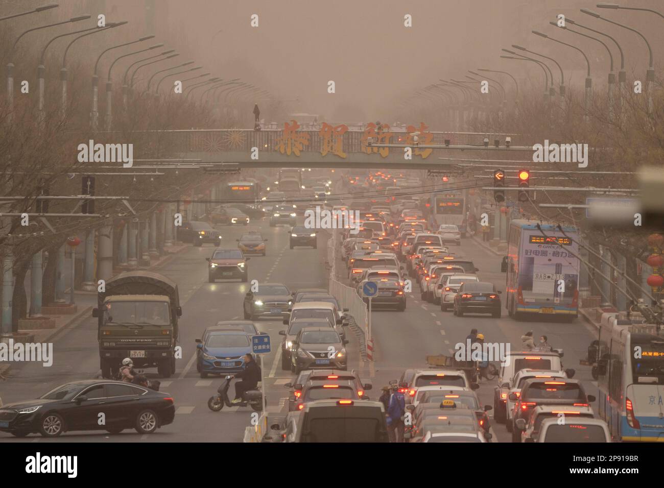 Cars and pedestrians navigate along a street shrouded in dust and haze ...
