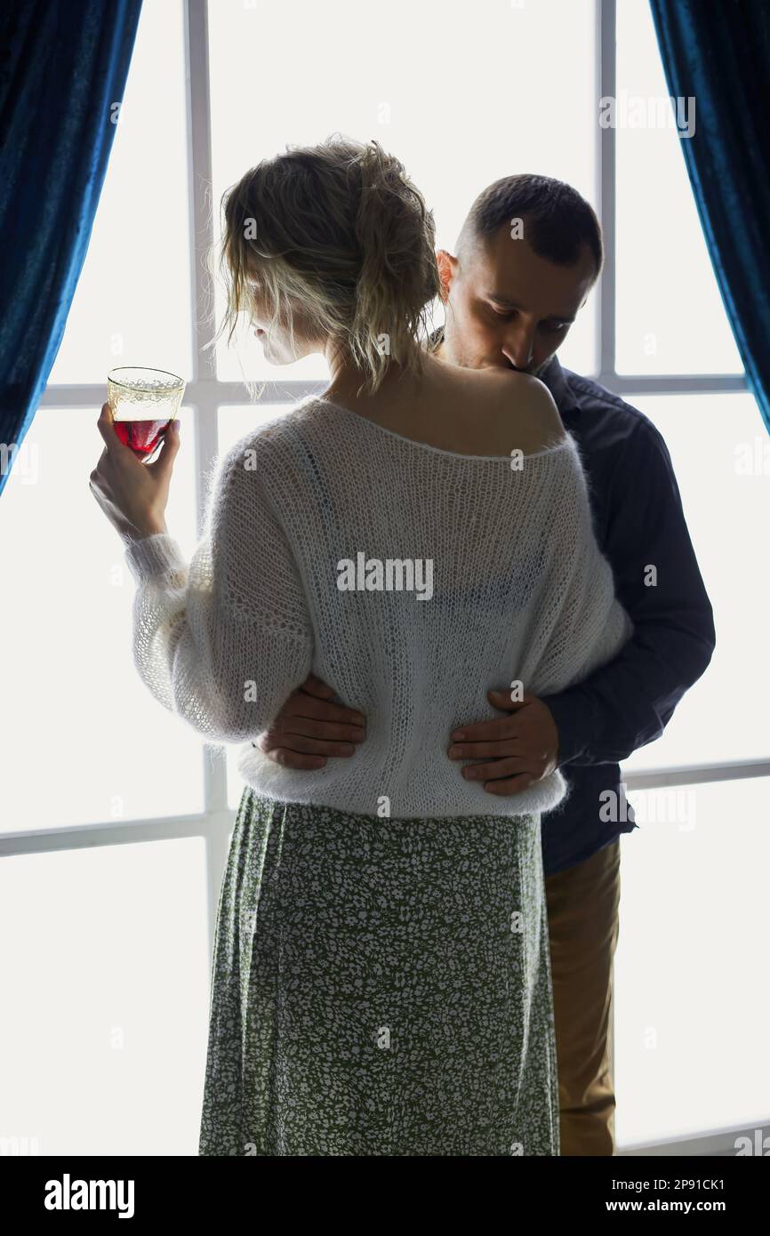 Stylish couple embracing in the dramatic lighting of a glowing window ...