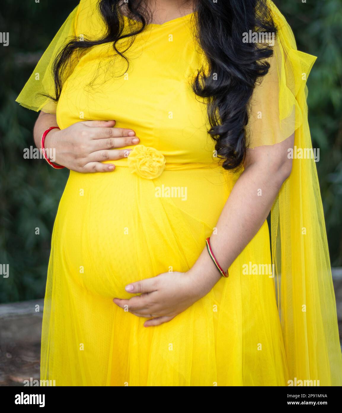 young pregnant women showing her round belly womb with hand in yellow ...