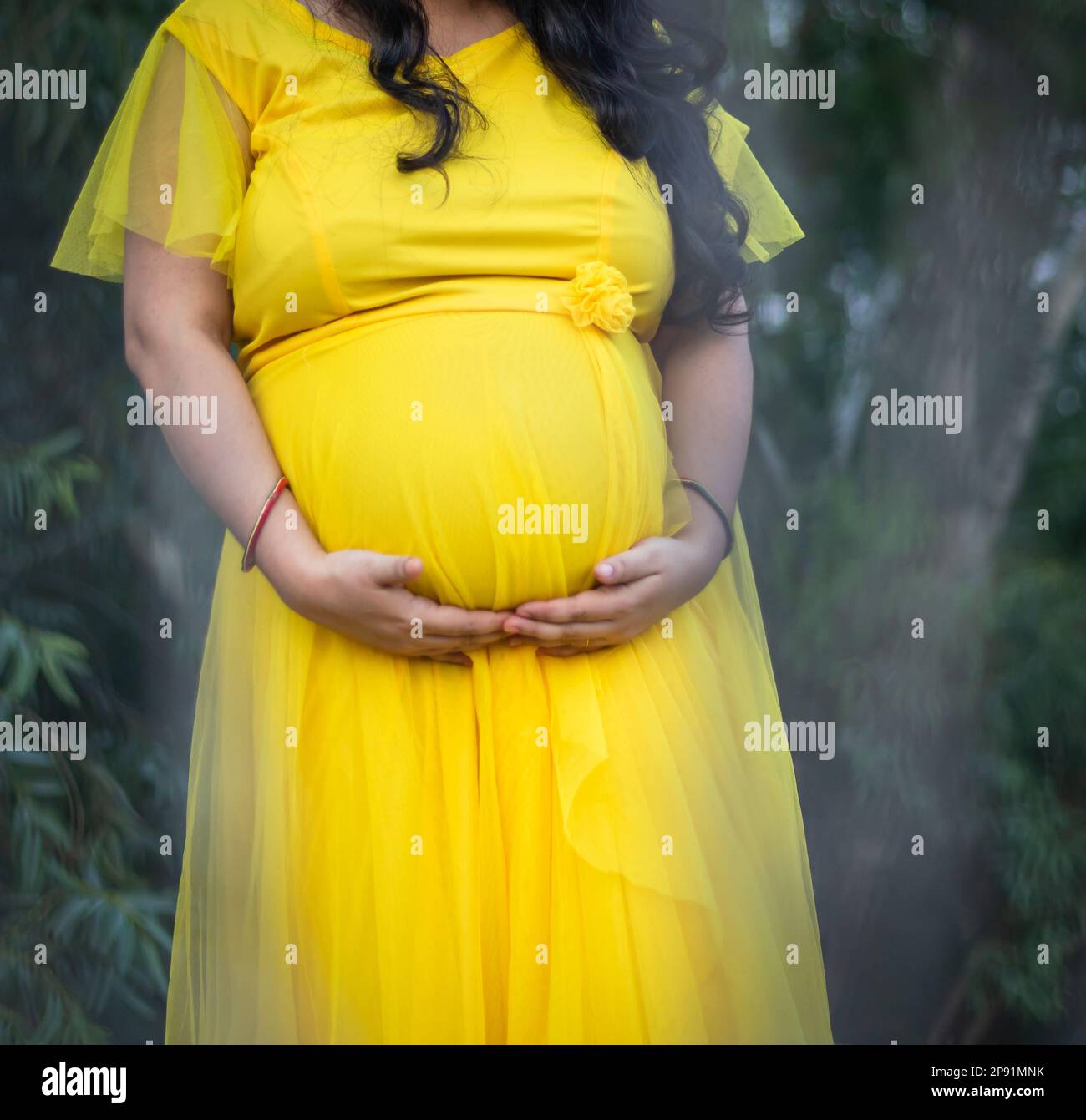 young pregnant women showing her round belly womb with hand in yellow ...