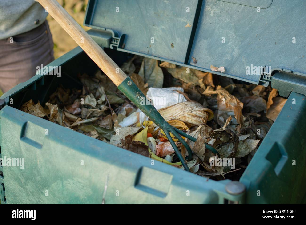 A young man is mixin the organic waste throwed to the outdoor compost ...