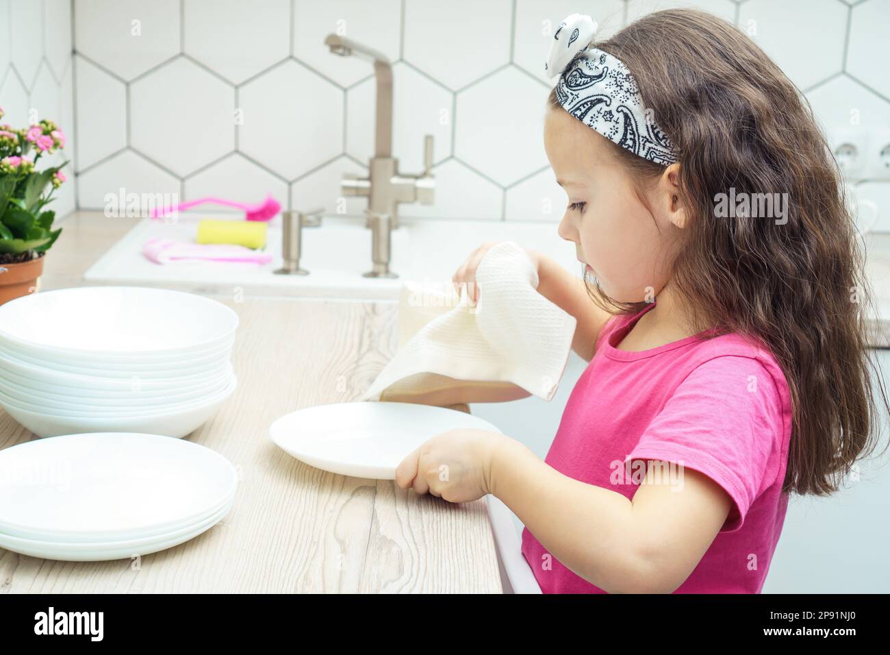 Pretty little girl wiping clear white plates with dry towel on kitchen ...
