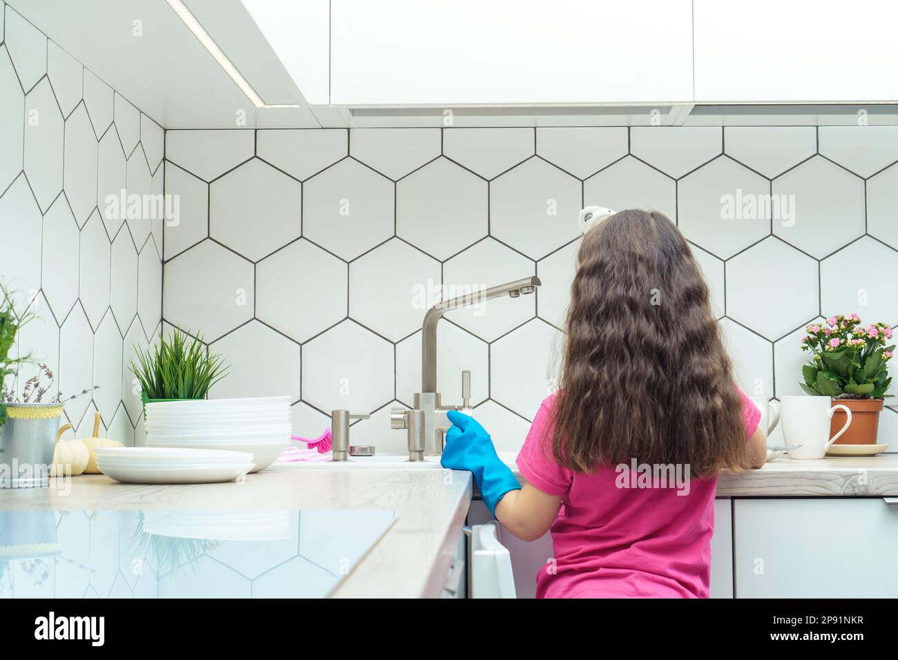 Little girl in protective gloves washing up dishes in kitchen sink ...
