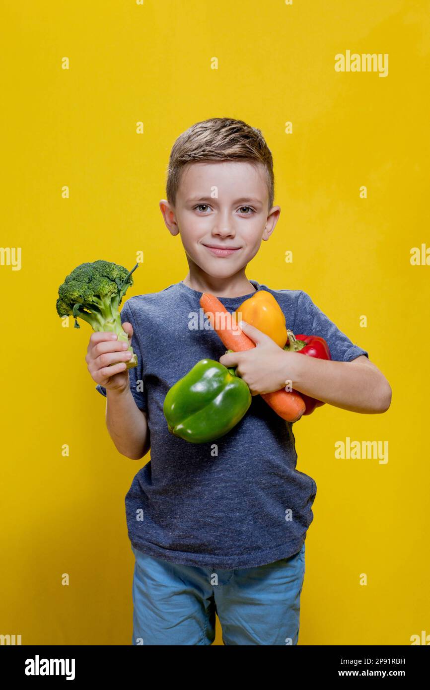 The boy holds fresh vegetables in his hands: broccoli, carrots and ...
