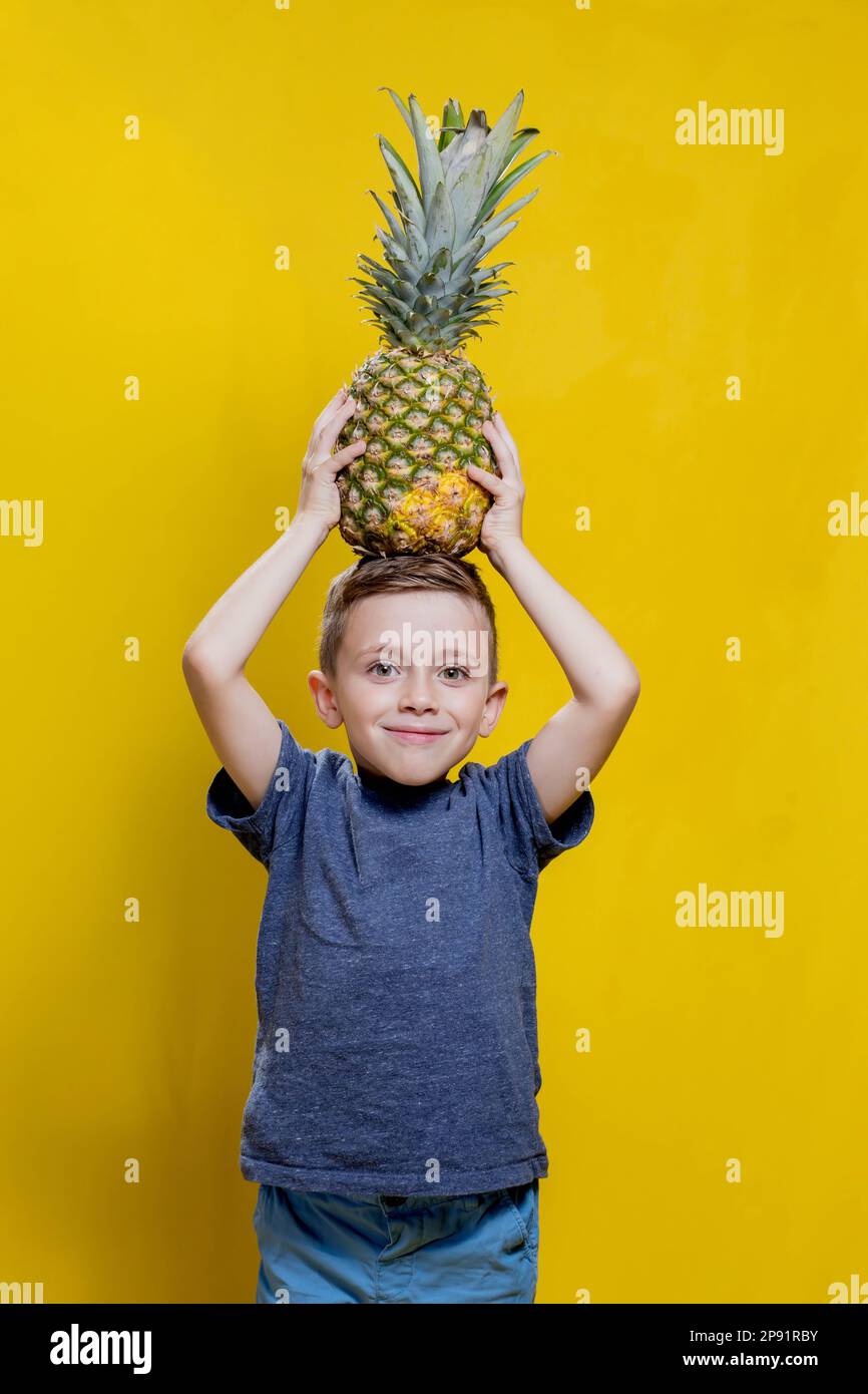 Child boy holding pineapple while posing on yellow background with copy ...