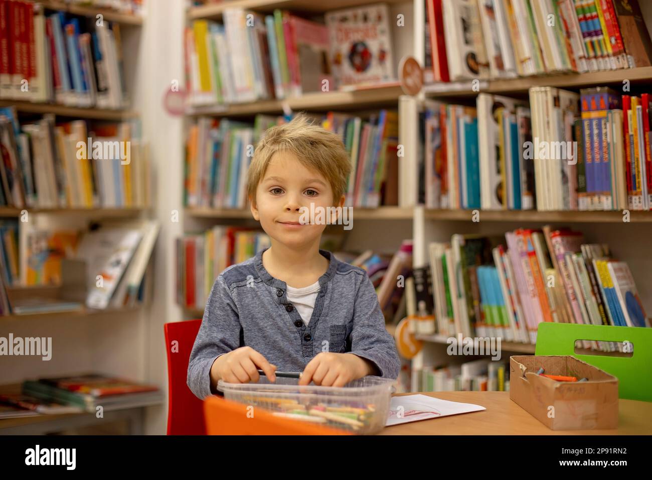 Adorable little child, boy, sitting in library, reading book and ...