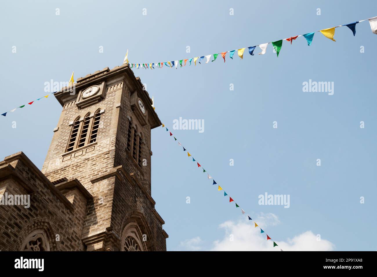 Old catholic church tower with a clock, decorated with colorful flags ...