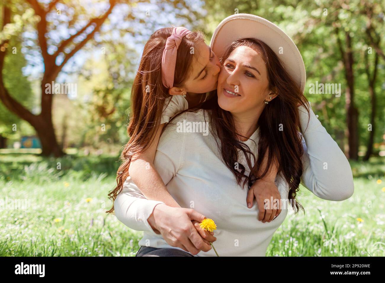 Girl kisses mother on cheek hugging while sitting on grass in spring ...