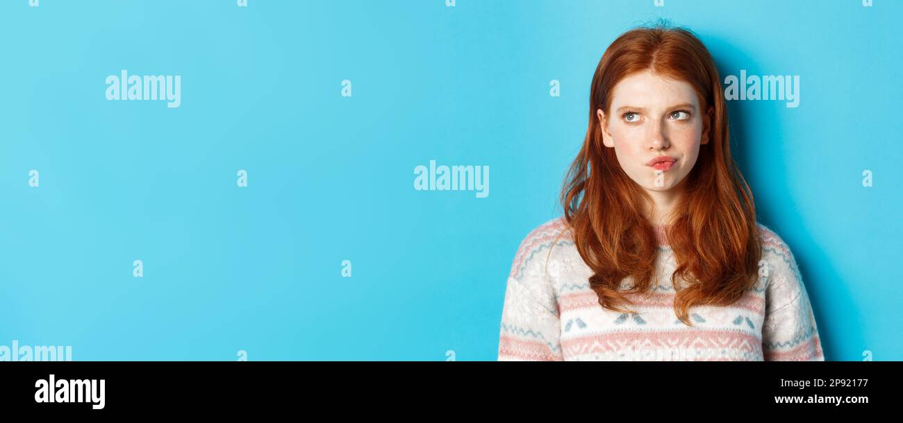 Serious redhead girl thinking, grimacing and frowning while pondering ...